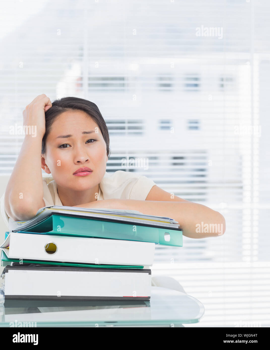 Portrait of a bored young businesswoman with stack of folders at office ...