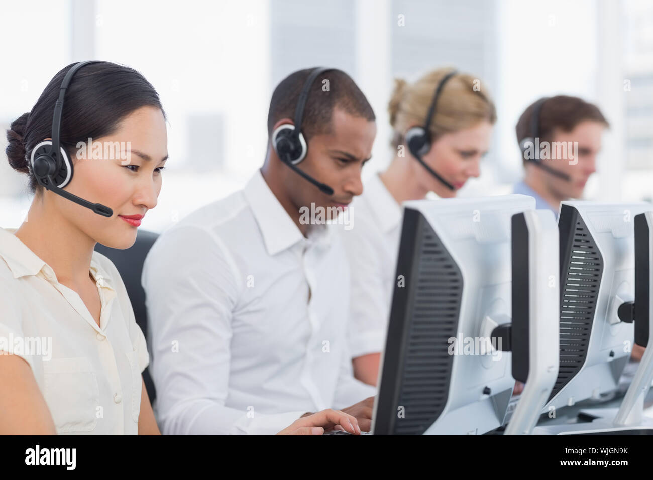 Group of business colleagues with headsets using computers at office ...