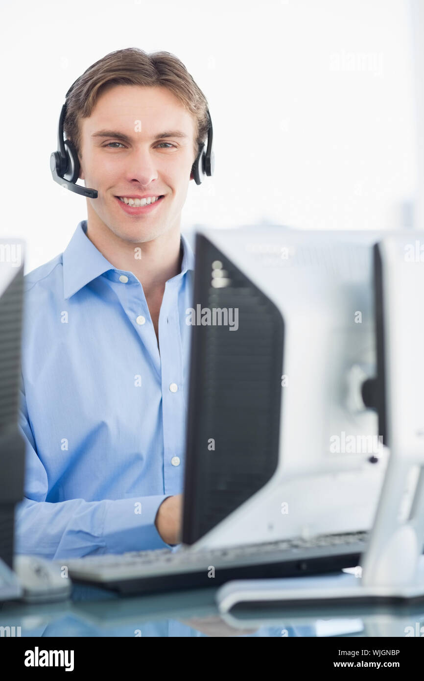 Portrait of a smiling male executive with headset using computer at ...