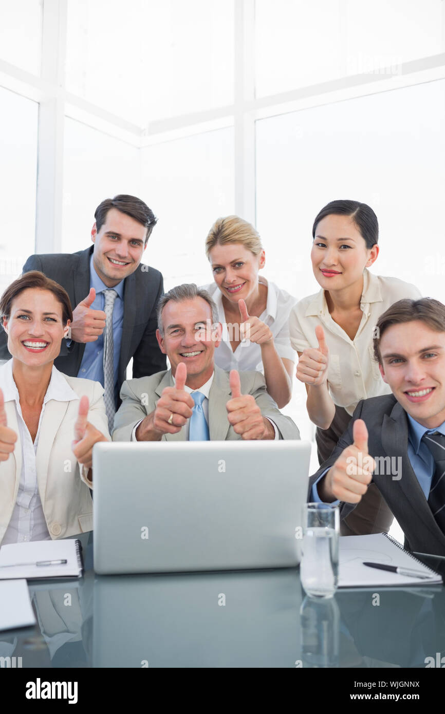 Group of happy business colleagues with laptop gesturing thumbs up at ...