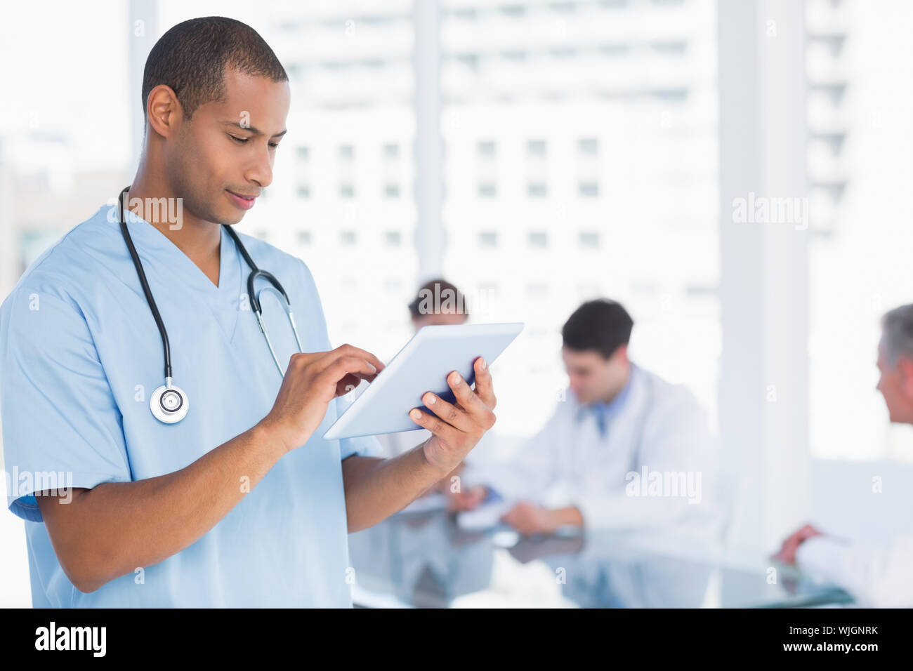 Male surgeon using digital tablet with group around table in background ...