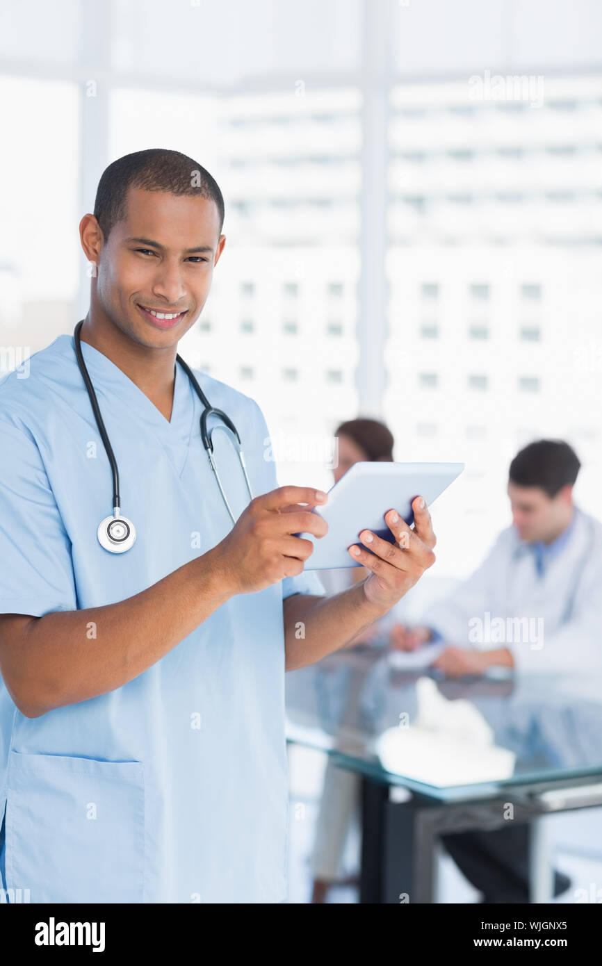 Male surgeon using digital tablet with group around table in background ...