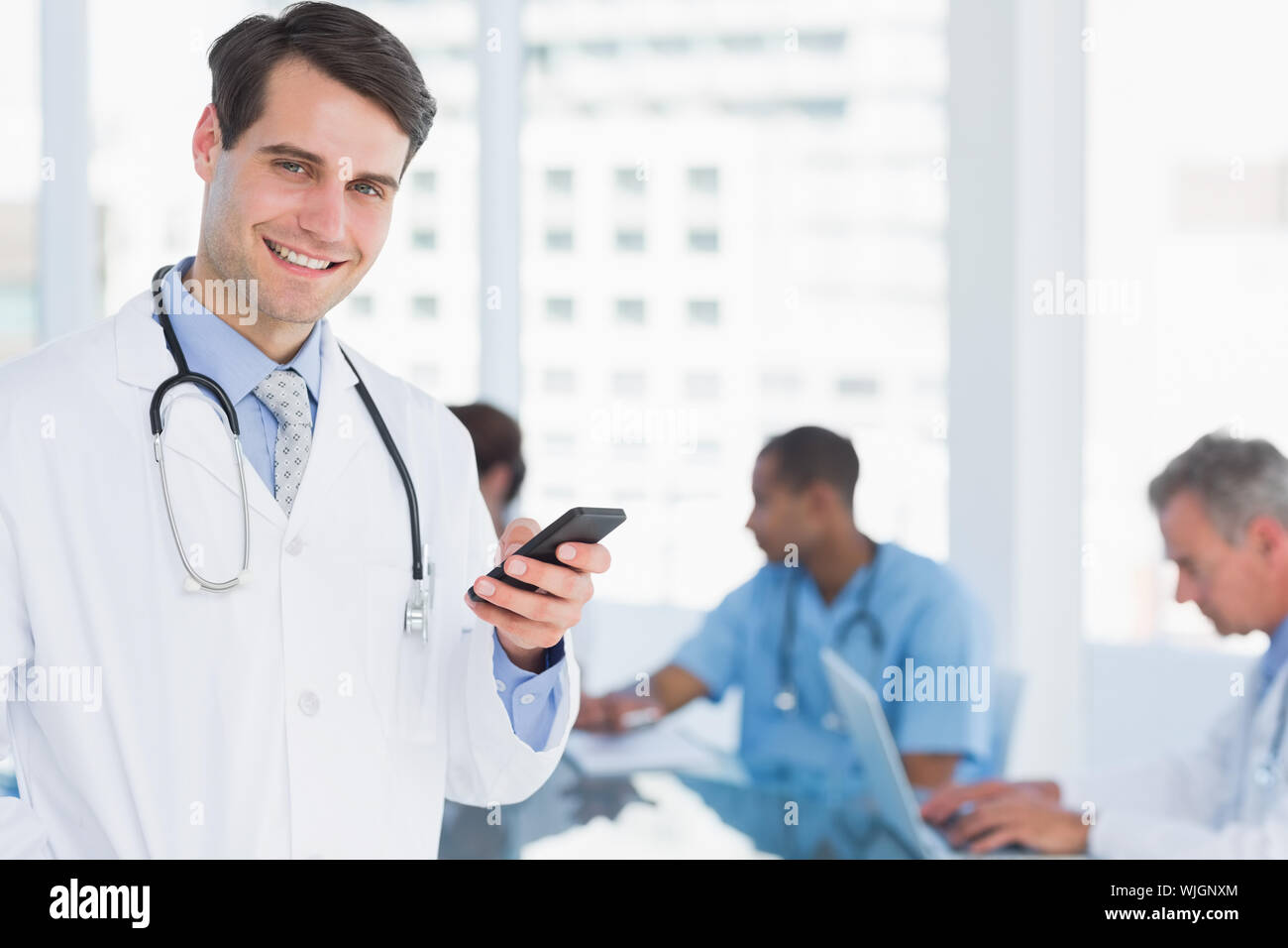 Doctor text messaging with group around table in background at hospital ...