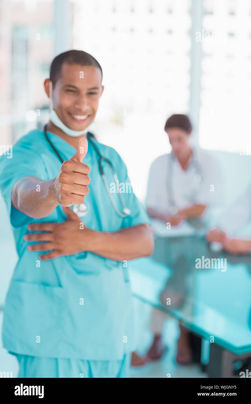 Smiling male surgeon gesturing thumbs up with group around table in ...