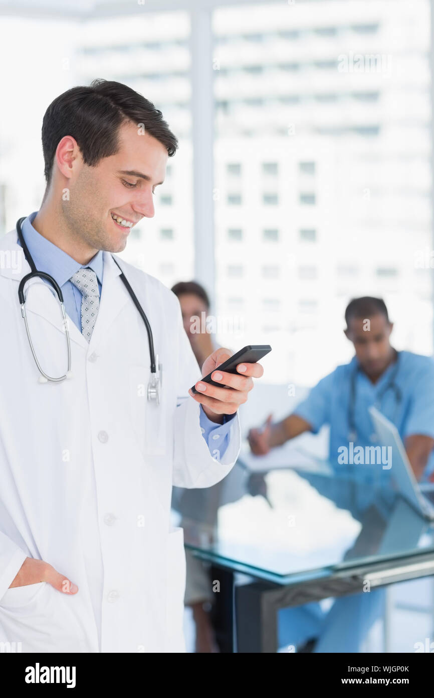 Doctor text messaging with group around table in background at hospital ...