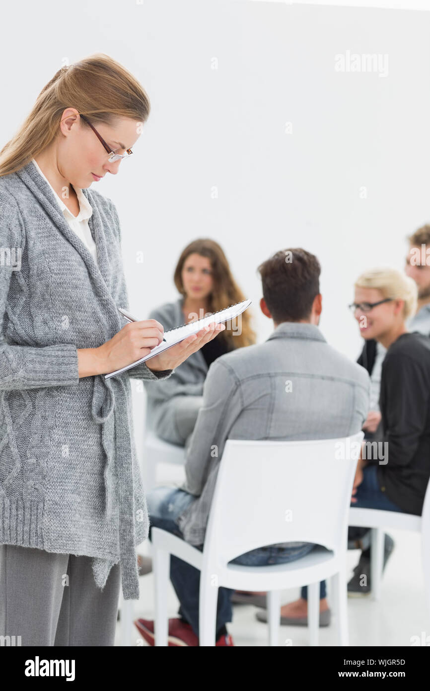 Serious female therapist writing notes with group therapy in session in ...