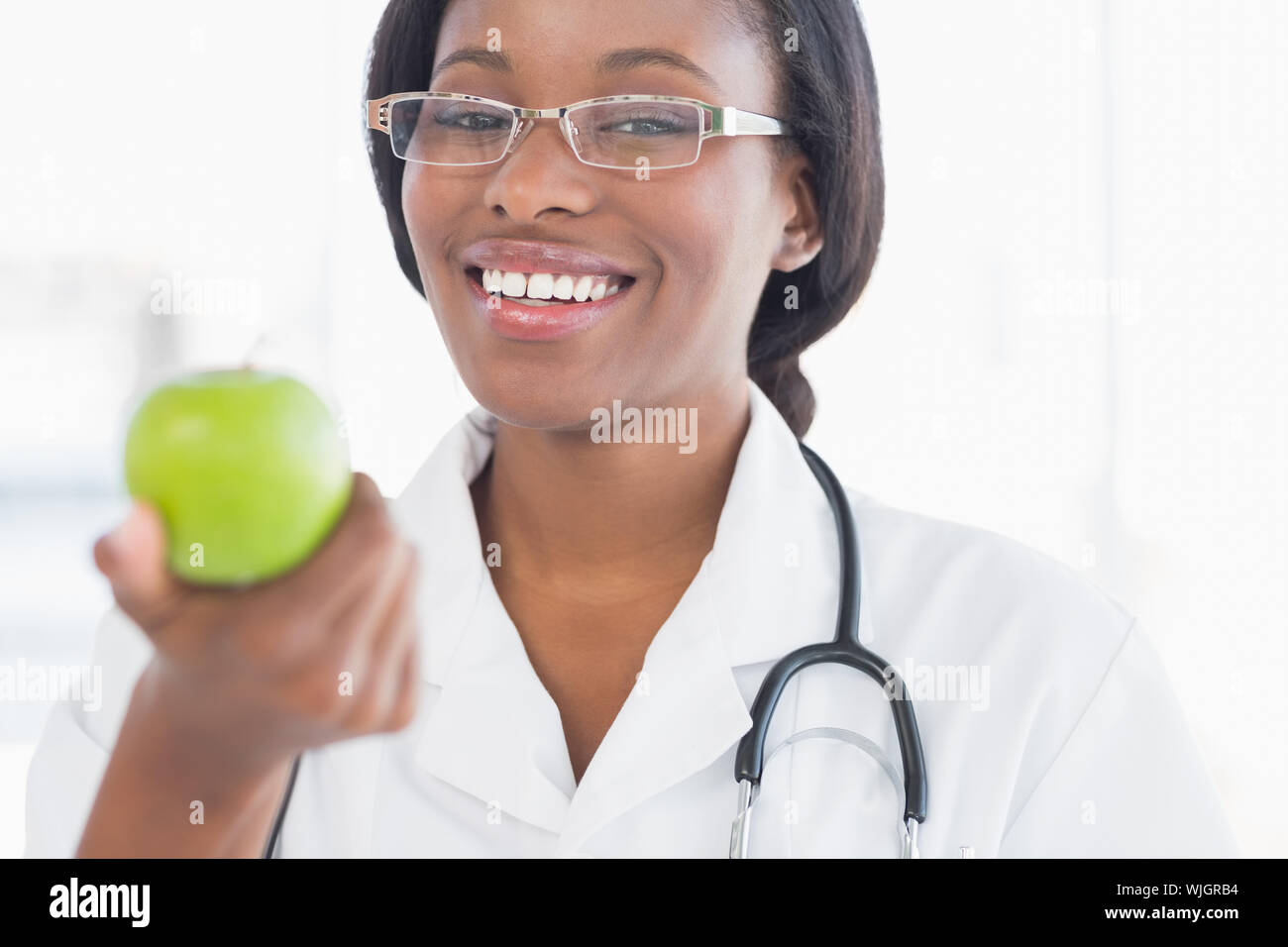 Portrait of a smiling female doctor holding an apple at a bright ...