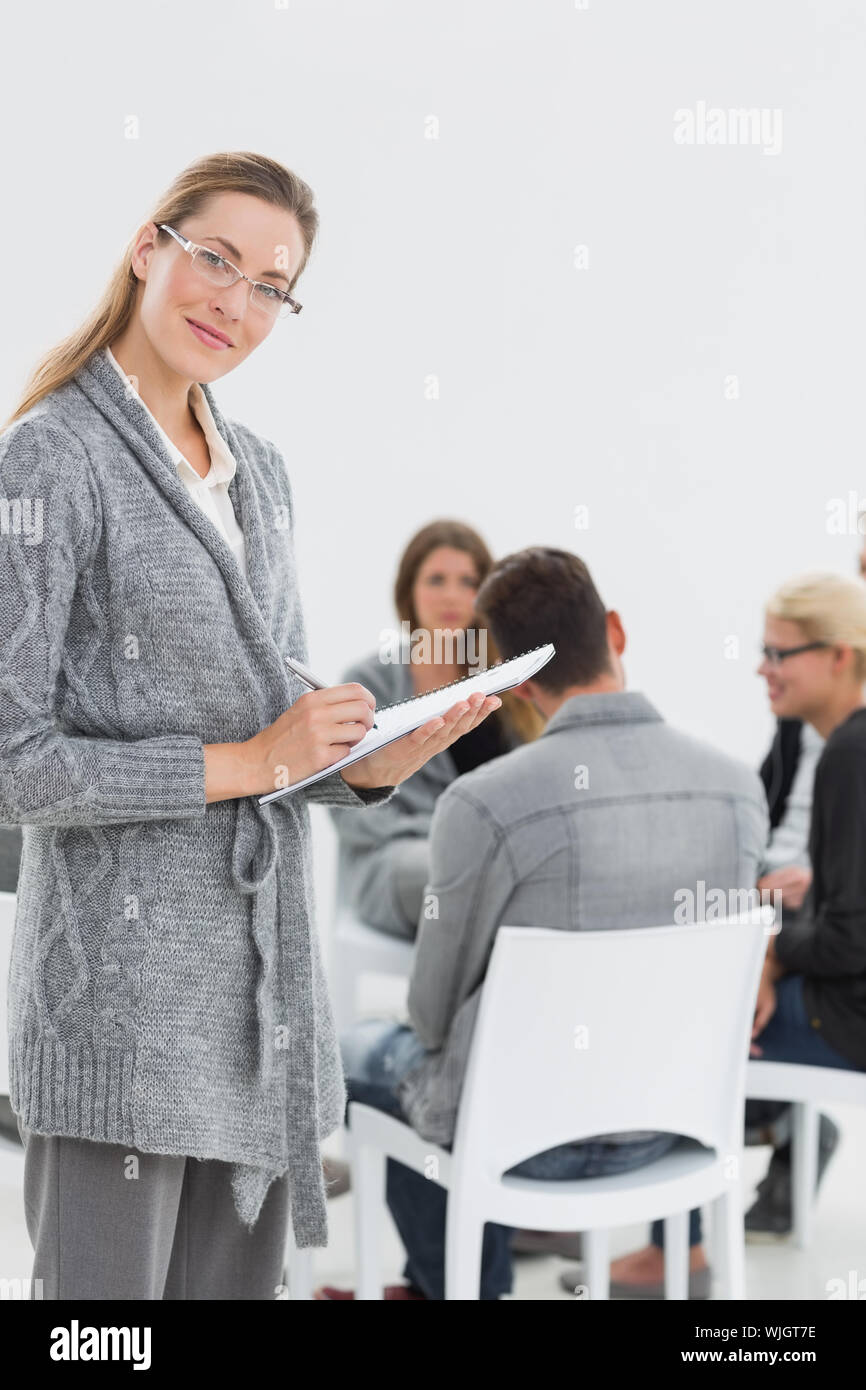 Portrait of a smiling female therapist with group therapy in session in ...
