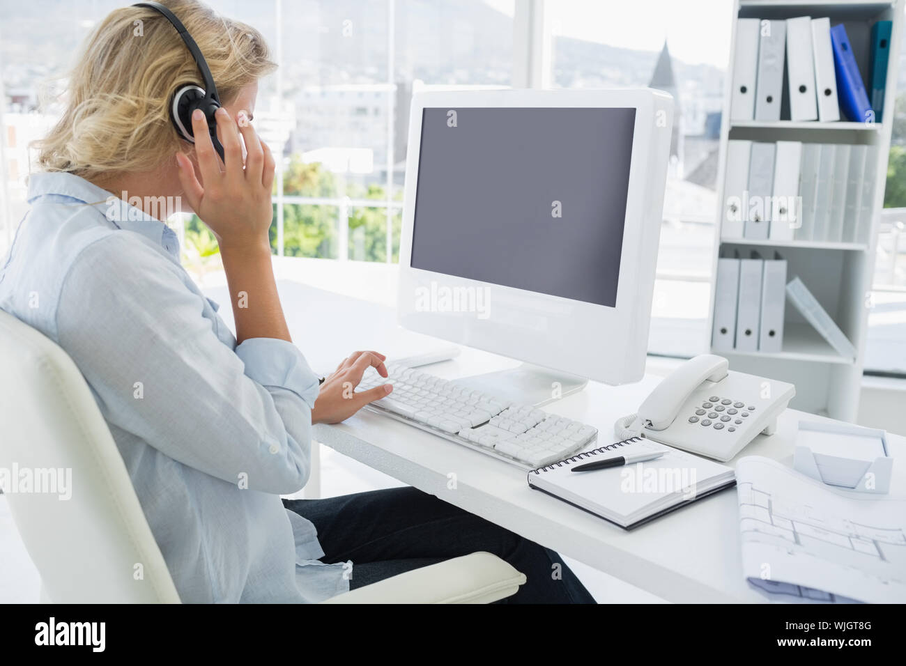 Side view of a casual young woman with headset using computer in a ...