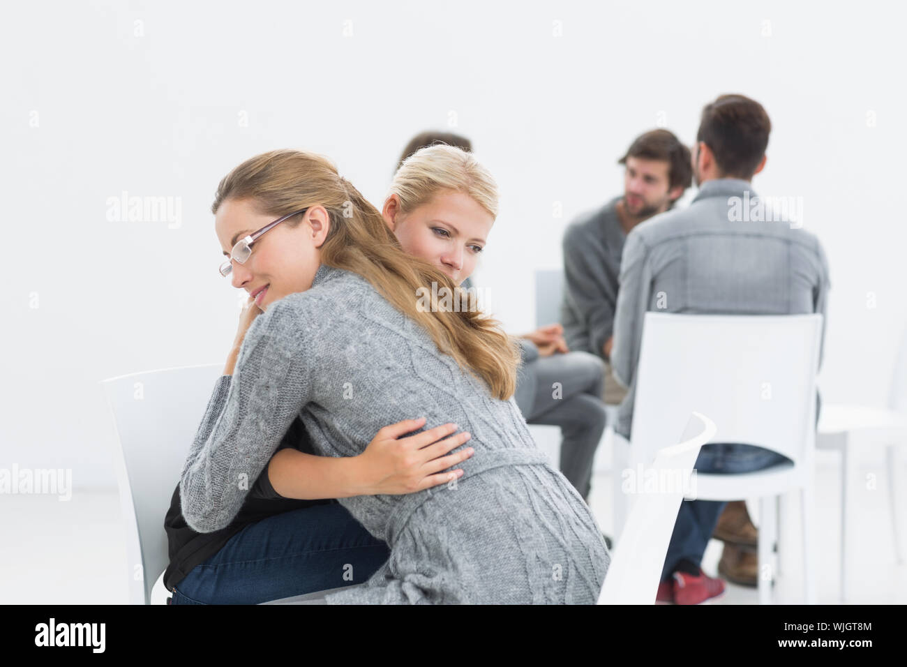 Group therapy session in circle with therapist and client hugging in ...