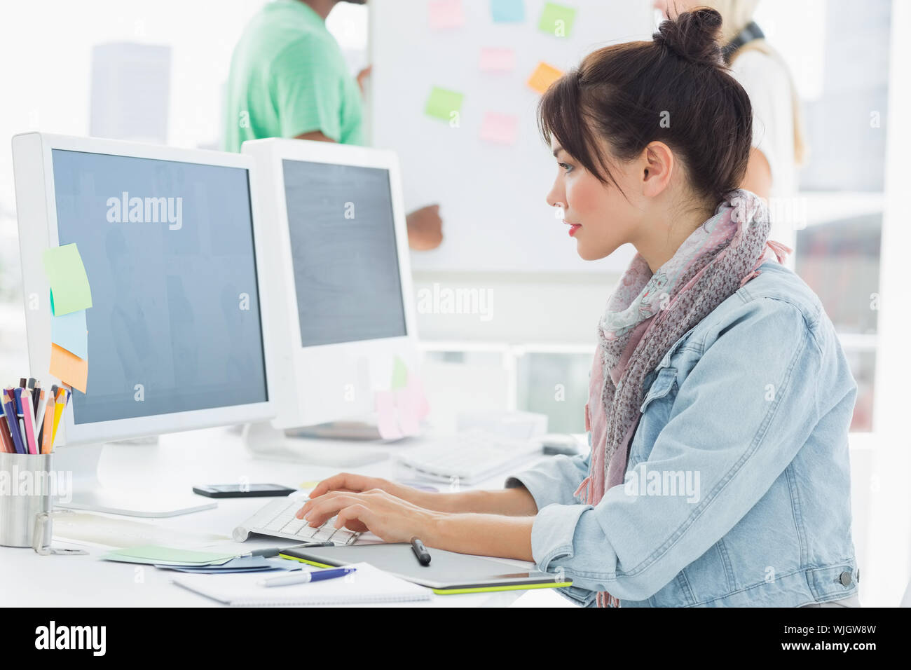 Side view of an artist using computer with colleagues behind at the ...
