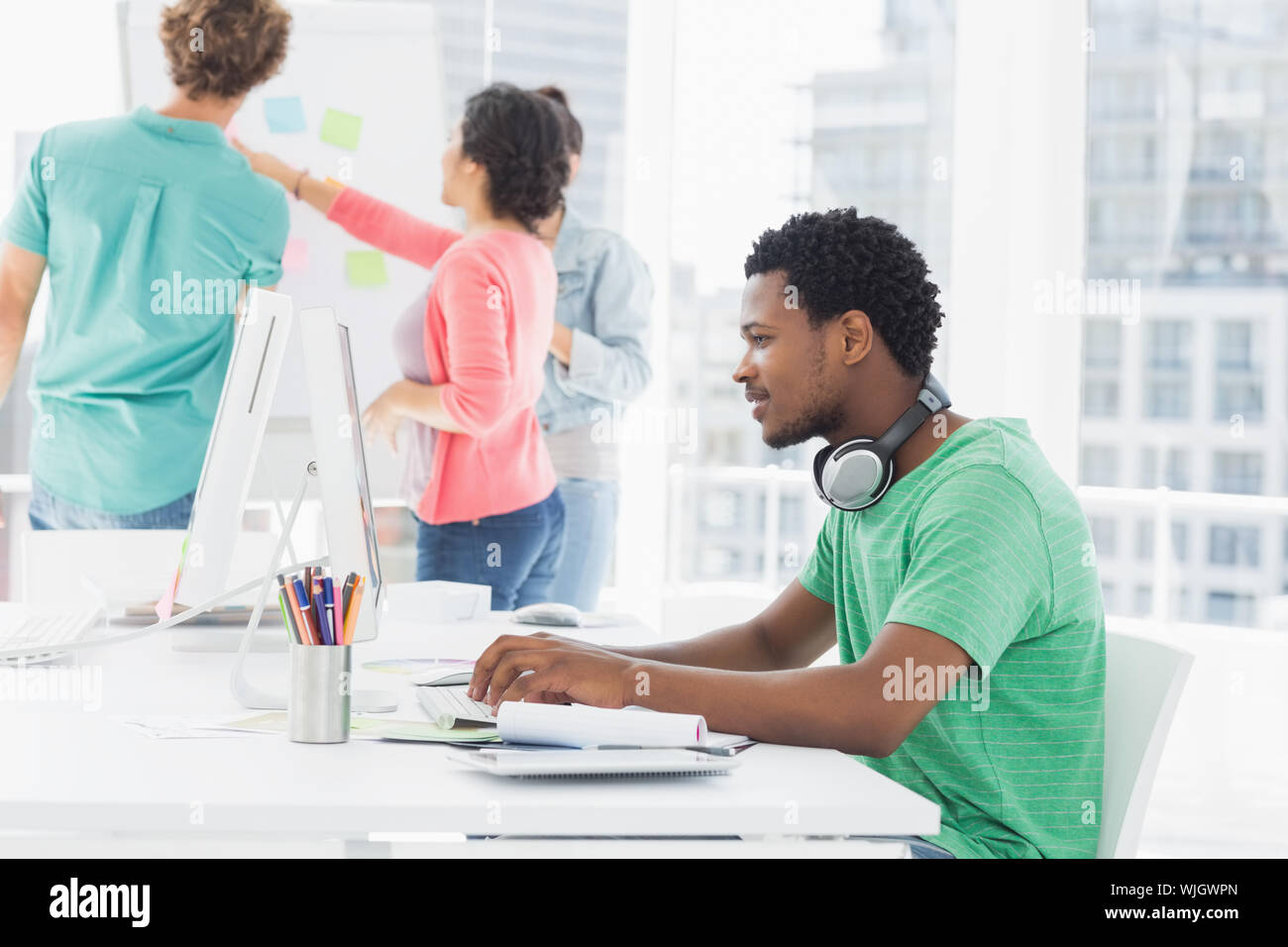 Side view of a casual man using computer with group of colleagues ...