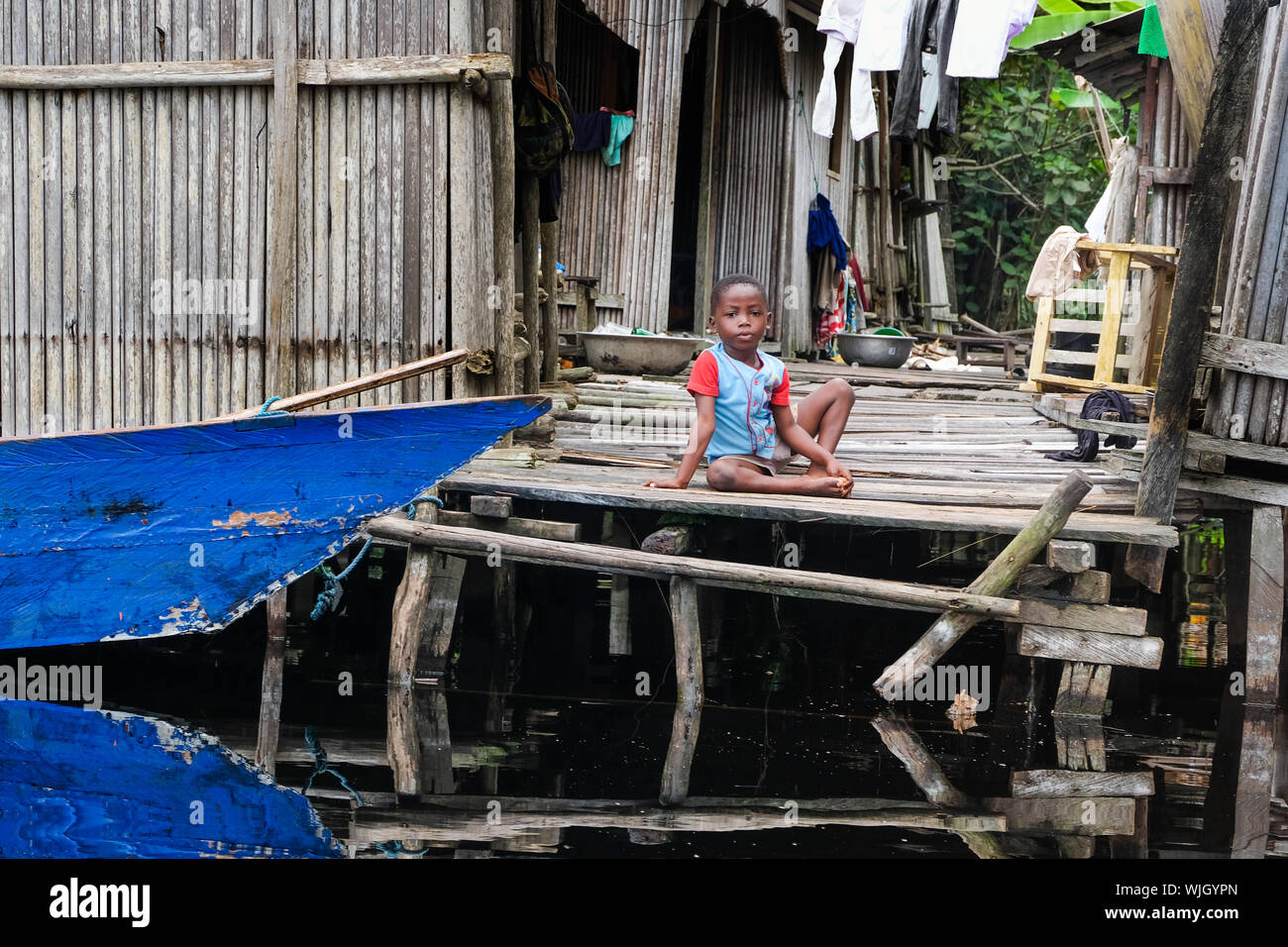 Child sitting at a boardwalk of Nzulezo stilt village, overlooks Lake ...