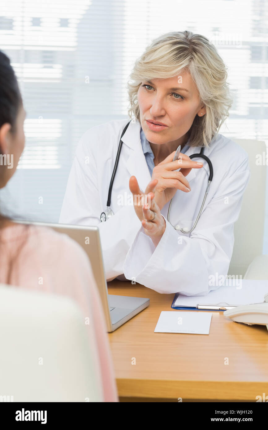 Female doctor listening to patient with concentration at desk in ...