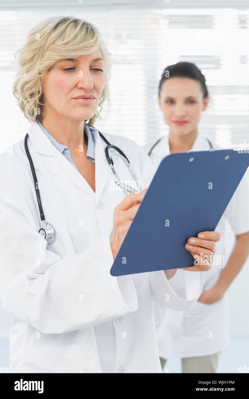 Concentrated female doctor reading reports with colleague in background ...