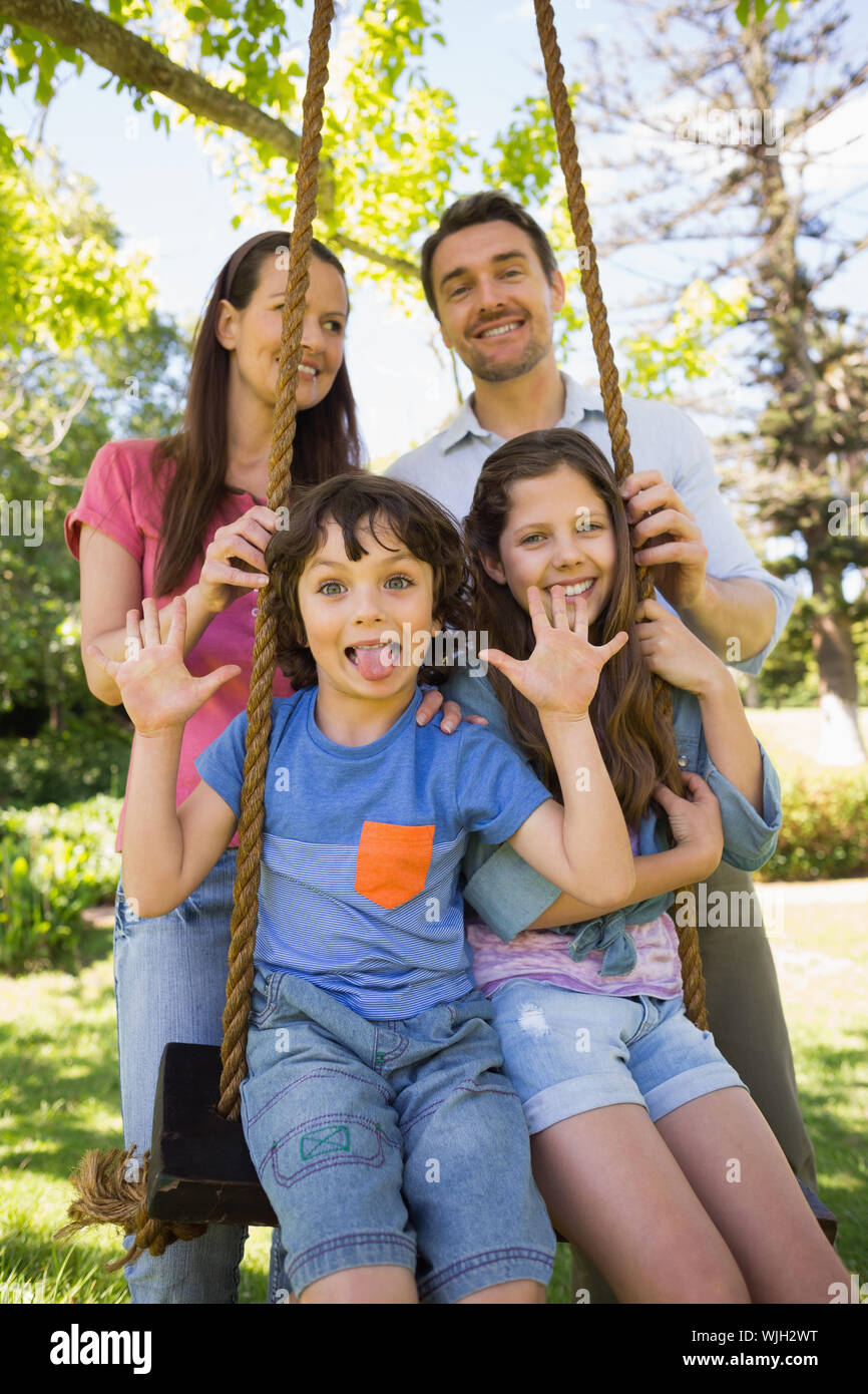 Happy couple pushing kids on swing in playground Stock Photo - Alamy