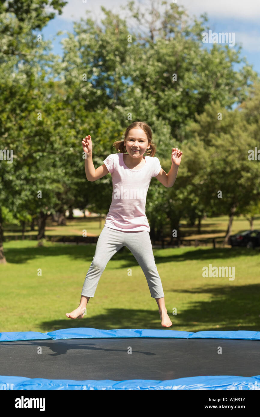 Full length of a happy girl jumping high on trampoline in the park ...
