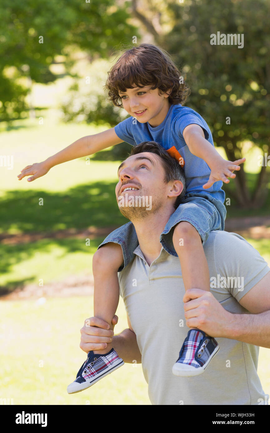 Side view of a smiling man carrying son on his shoulders in the park ...