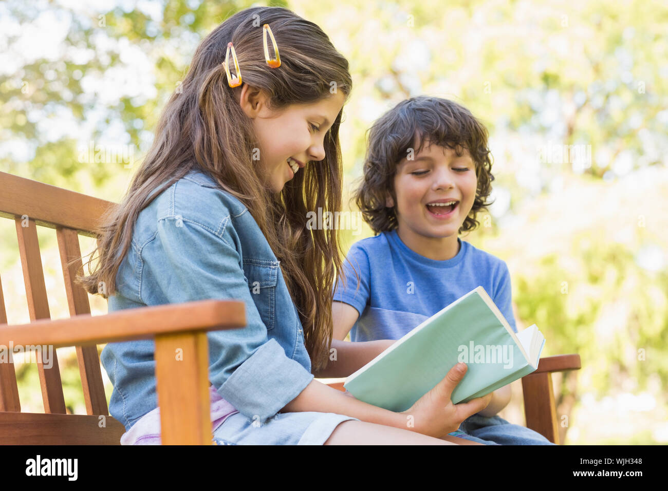 Side view of a young boy and girl reading book on park bench Stock ...