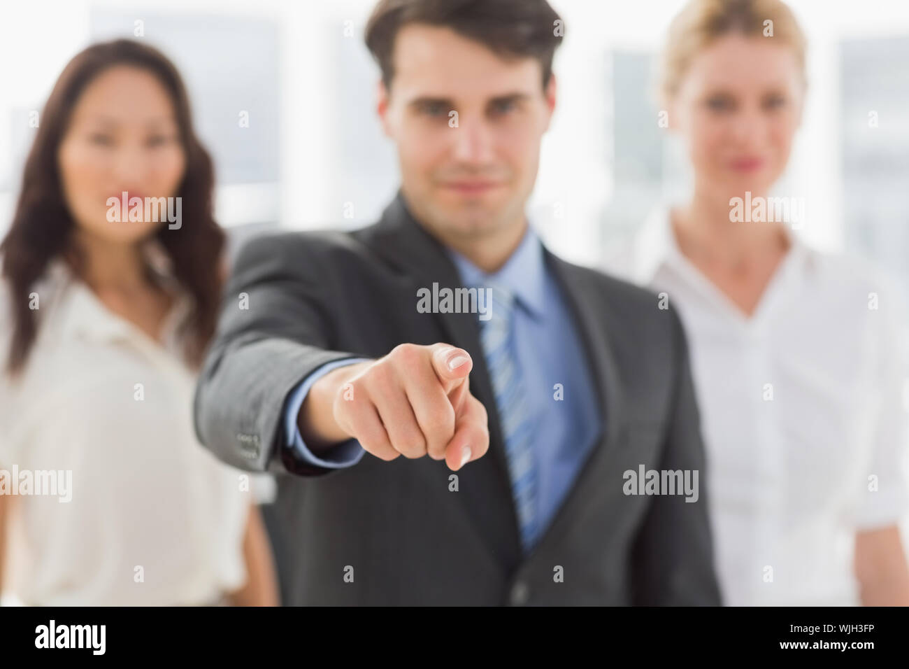 Smiling businessman pointing to camera in front of his team in the ...