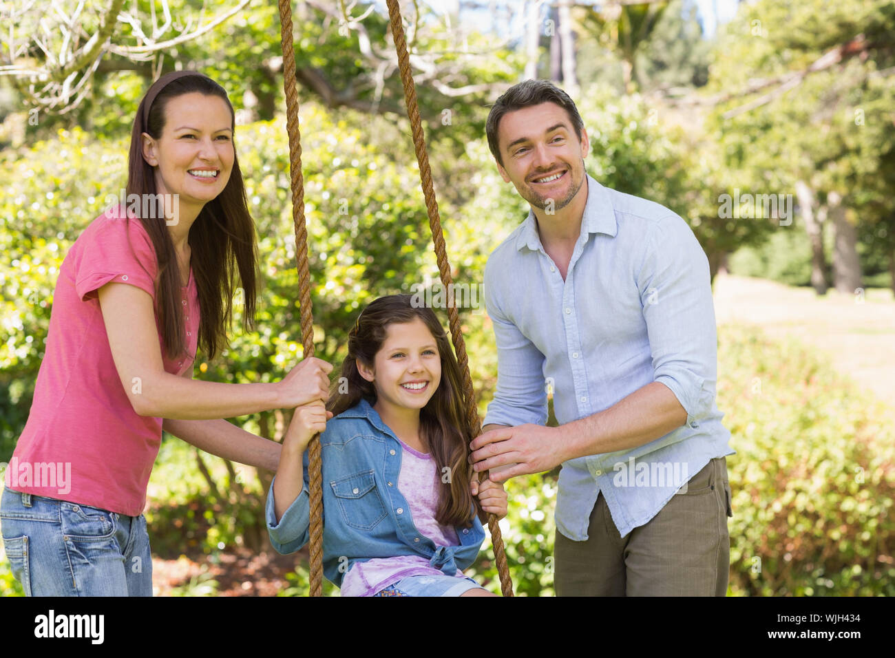 Happy couple pushing daughter on swing in playground Stock Photo - Alamy