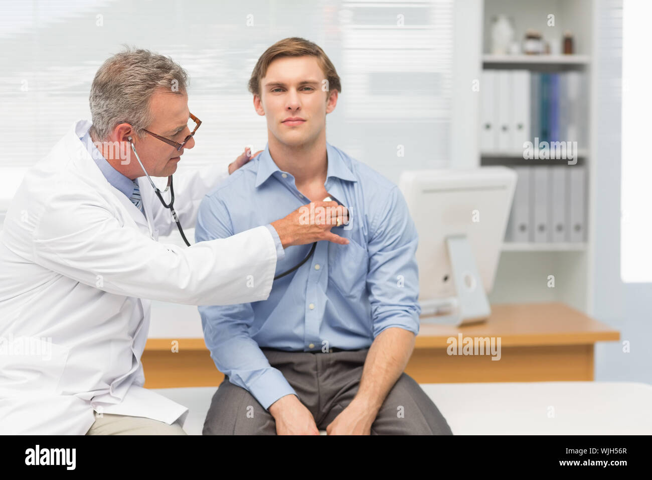 Mature doctor listening to his patients chest with stethoscope in his ...