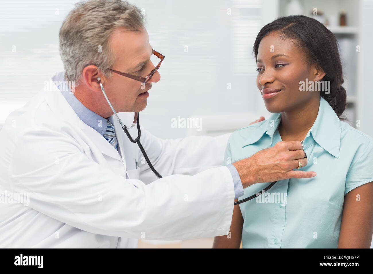 Doctor listening to cheerful young patients chest with stethoscope in ...