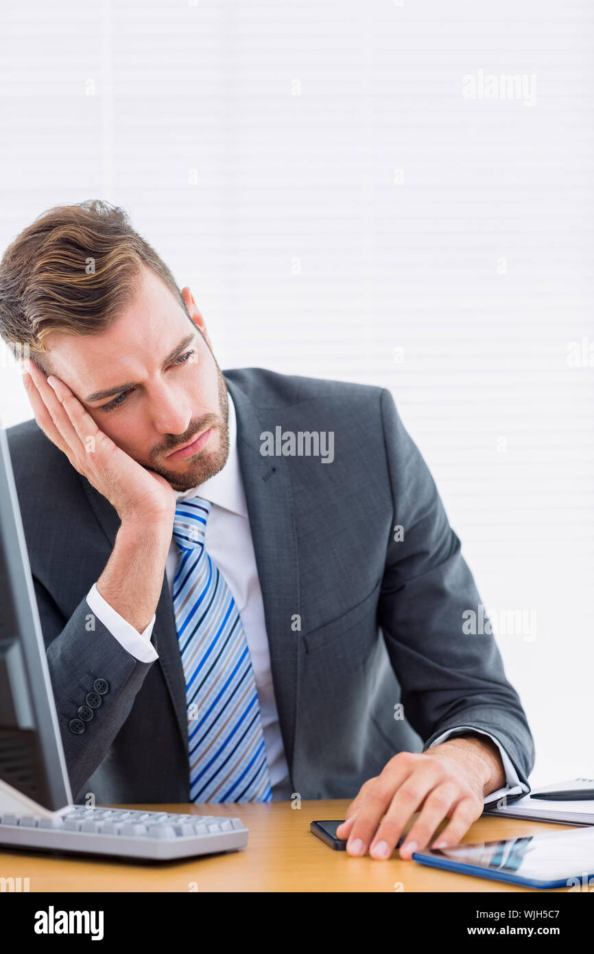 Young thoughtful businessman sitting by computer at office desk Stock ...