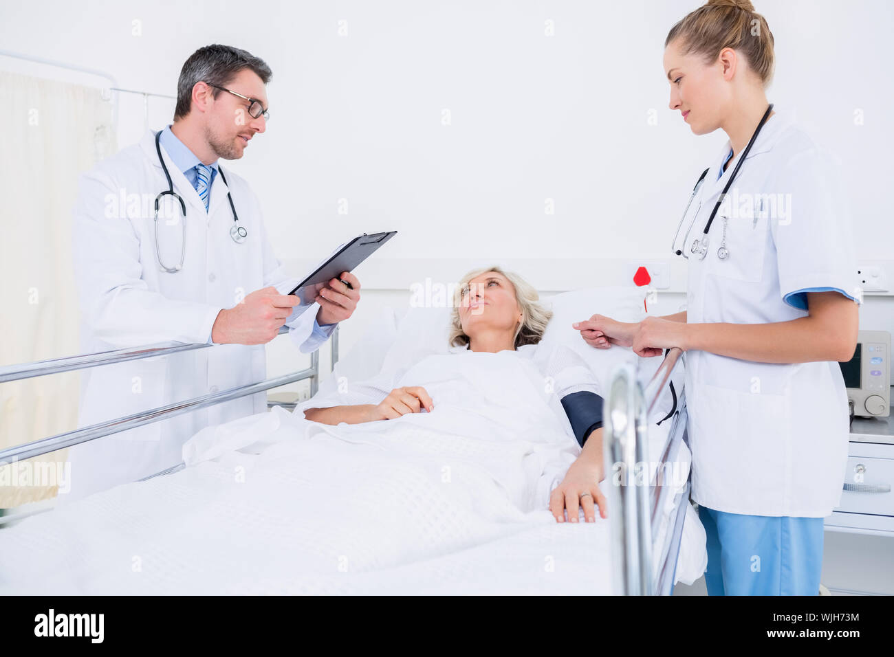 Side view of two doctors visiting a female patient in the hospital ...