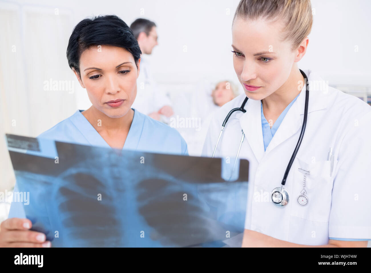 Doctor and surgeon examining x-ray with patient in background at the ...