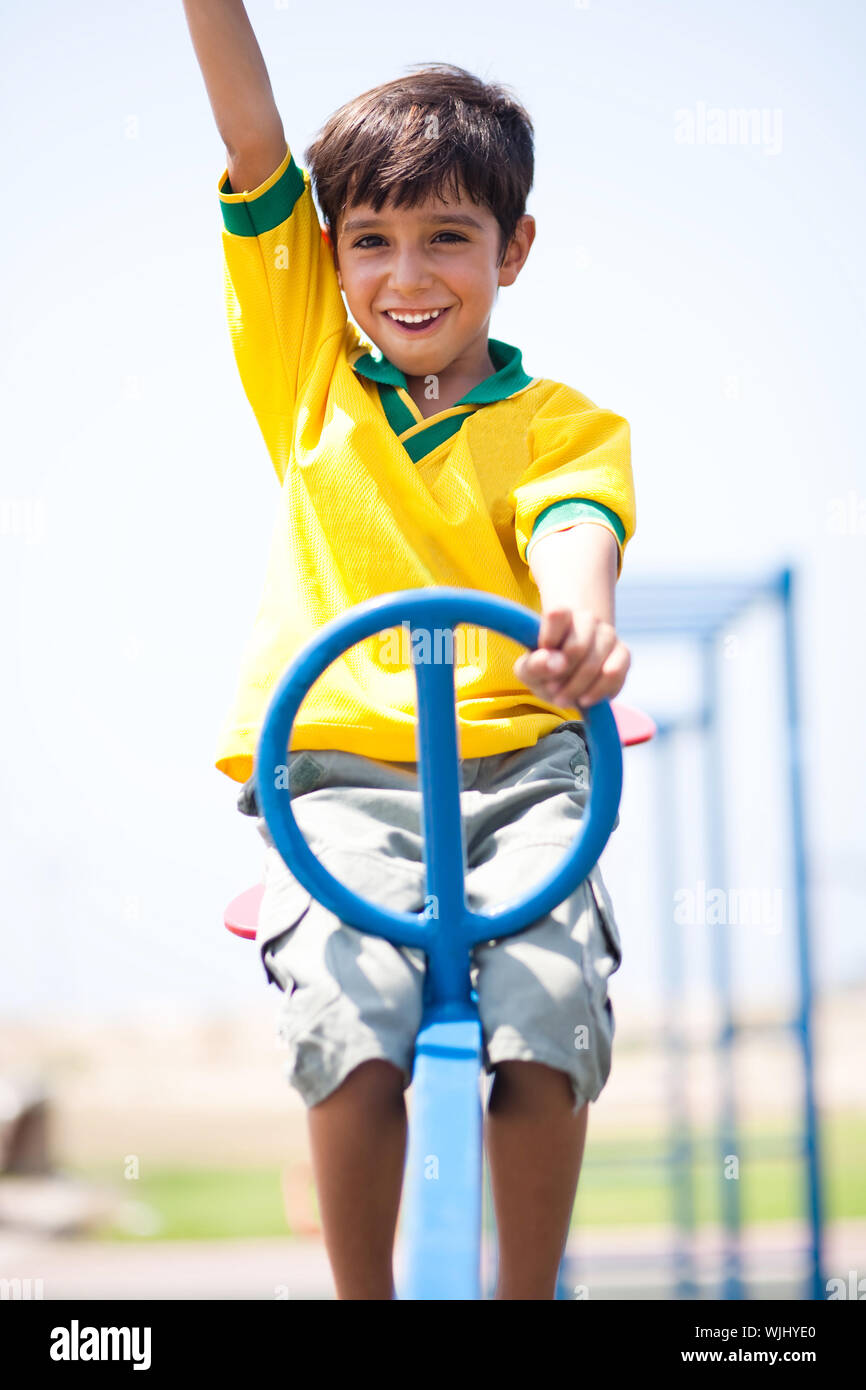 Boy in soccer uniform playing in the park and taking ride on swing ...