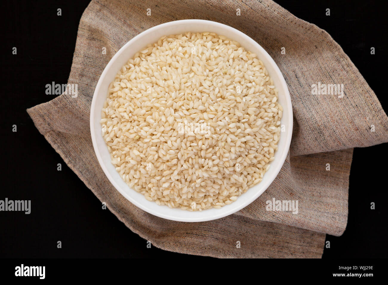 Organic Arborio rice in a white bowl on a black background, overhead ...