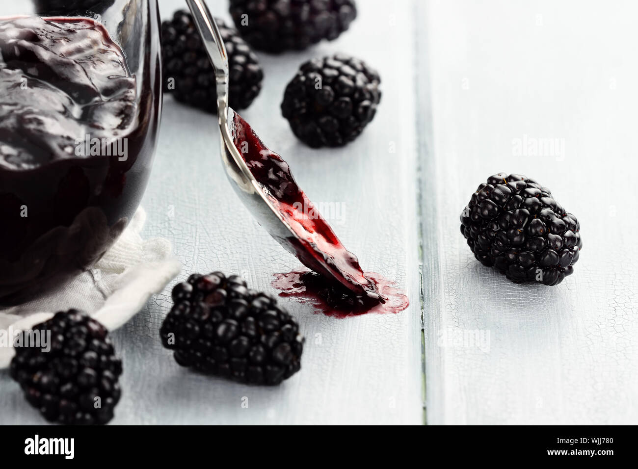 Messy spoon with blackberry jelly on a blue table. Extreme shallow ...