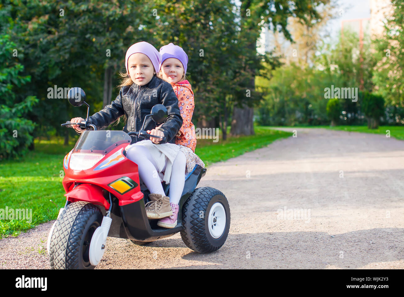 Adorable little girls riding on kid's motobike in the green park Stock ...
