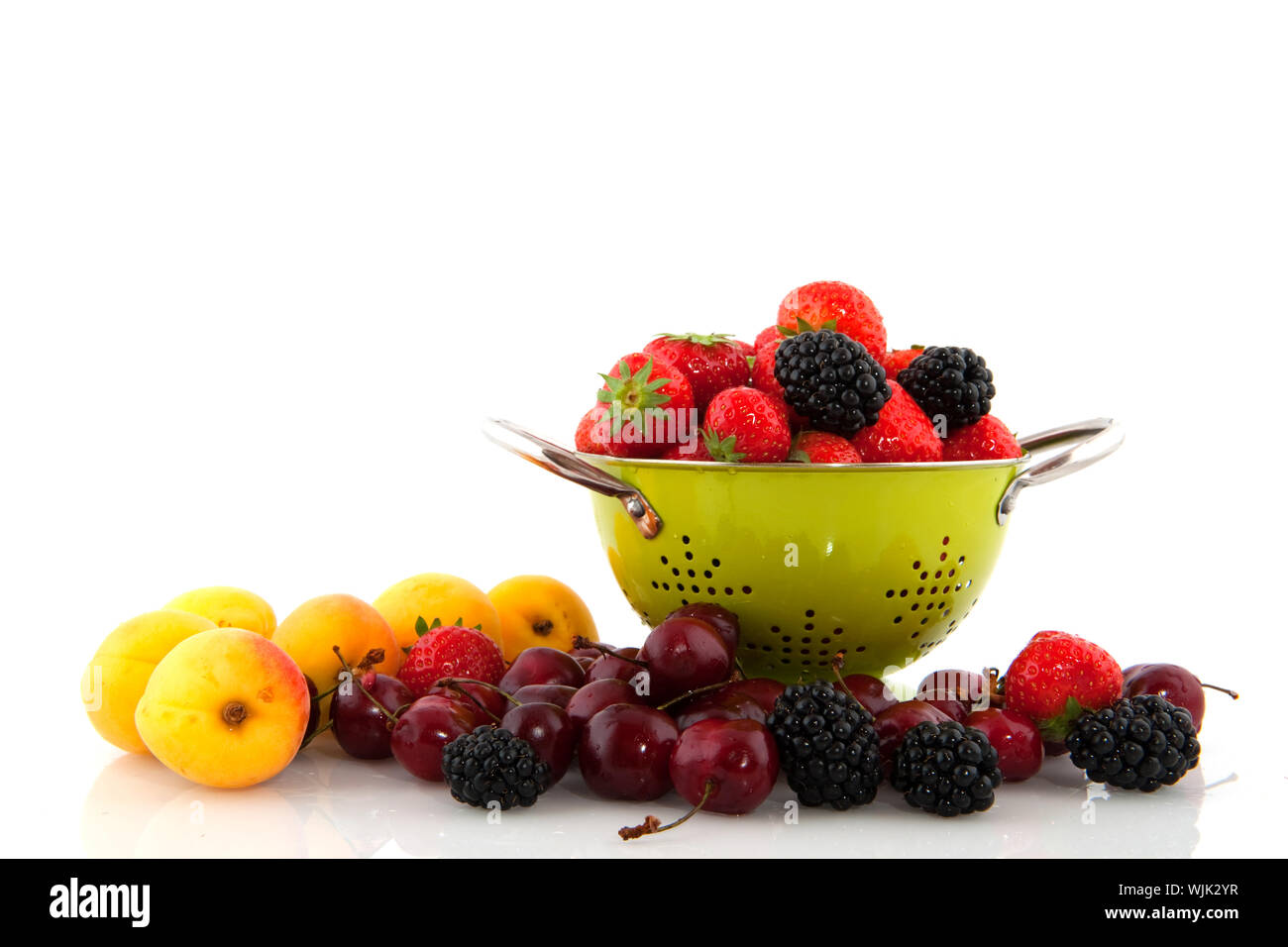 Green colander with cherries and strawberries isolated over white Stock ...