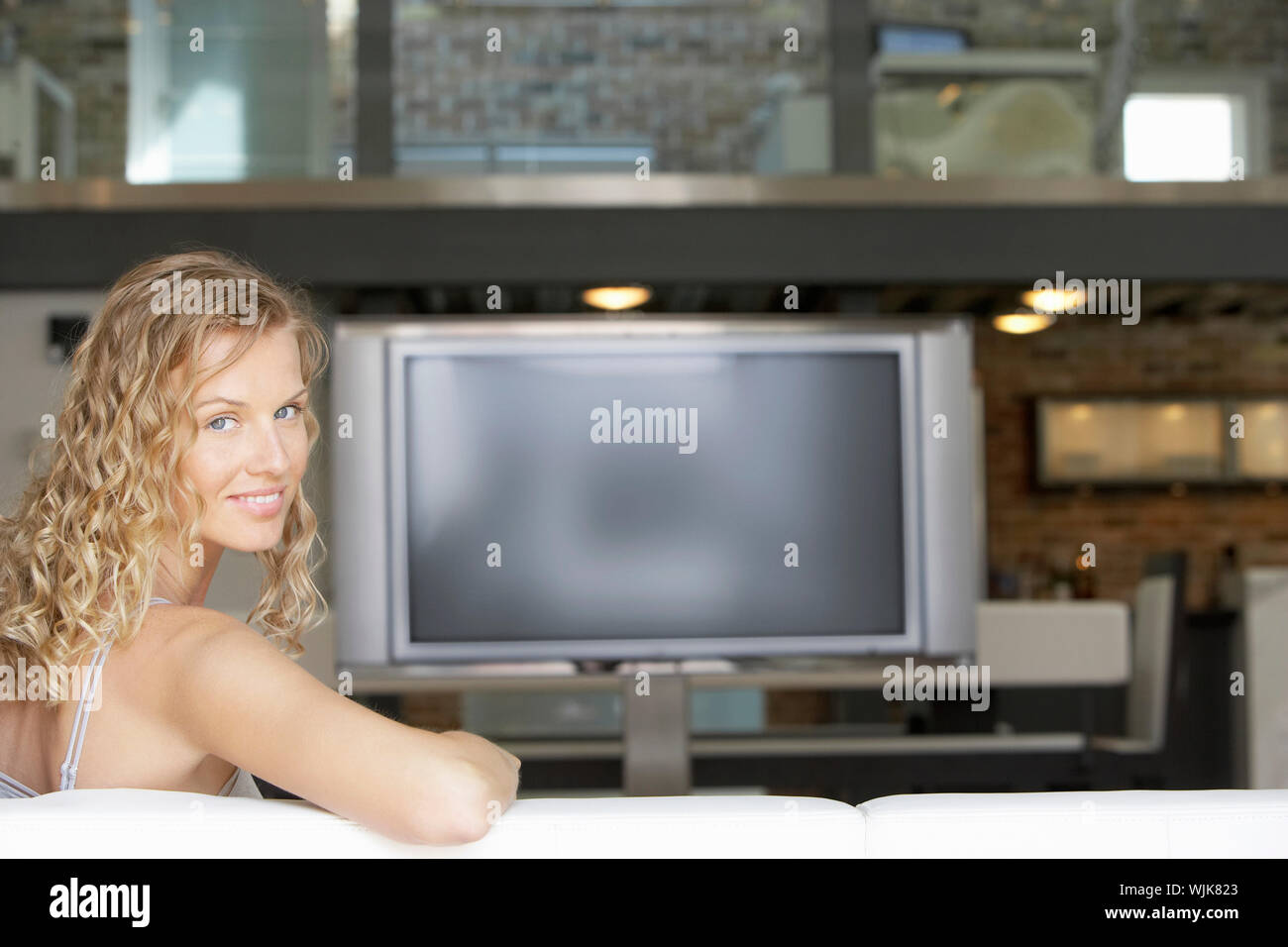 Portrait of beautiful young woman sitting in living room with plasma ...