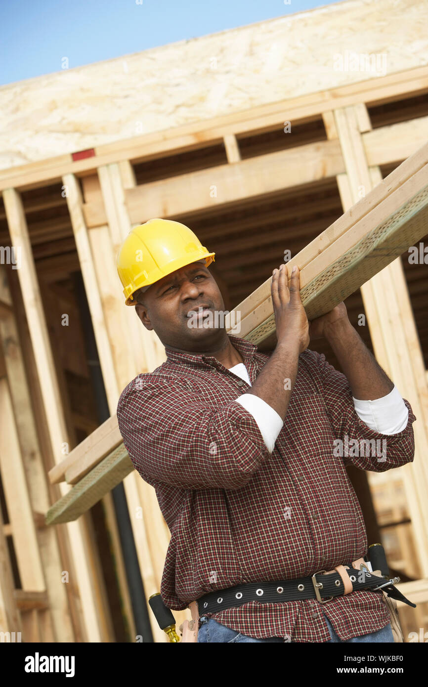 African American Construction Worker Carrying Lumber On Job Site Stock