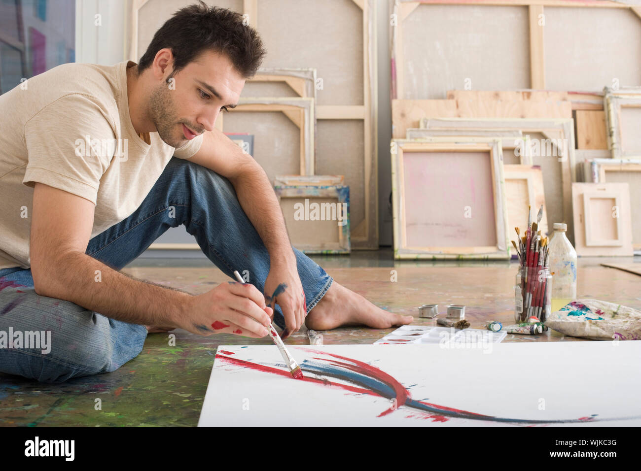 Side view of a young man painting on canvas on studio floor Stock Photo ...