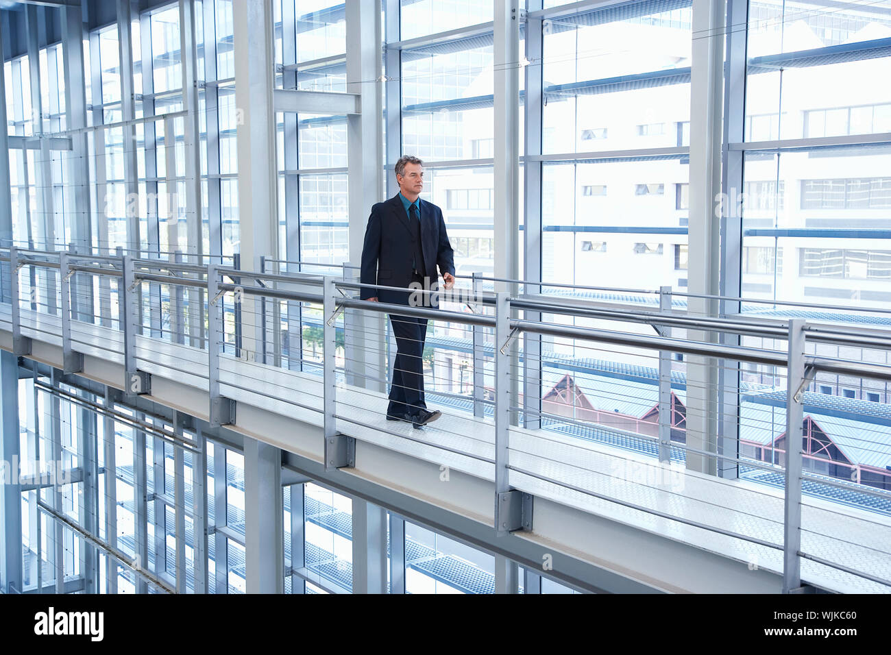 Full length of middle aged businessman walking by railing in modern ...