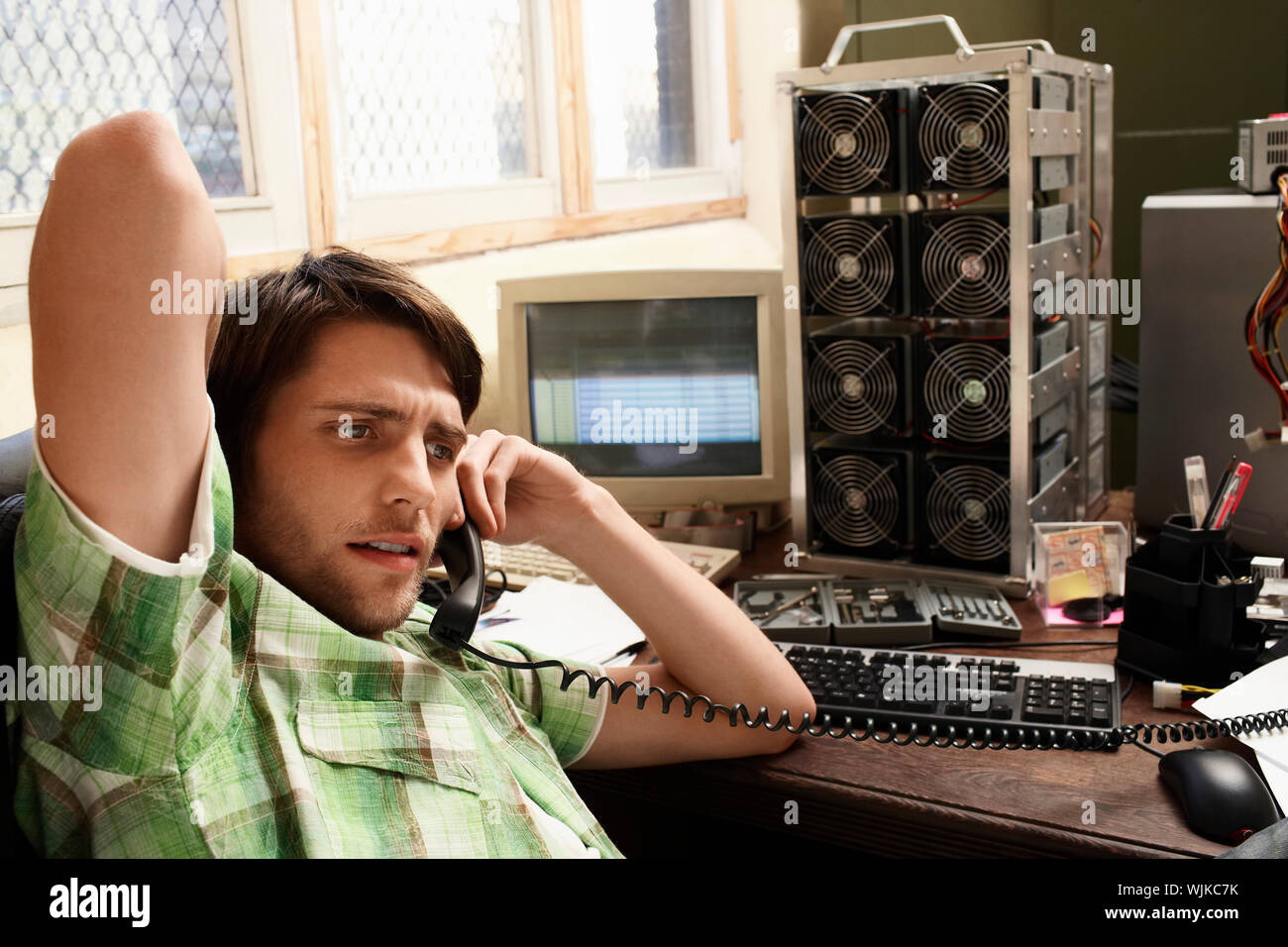 Young man using landline phone surrounded by computer equipment Stock ...