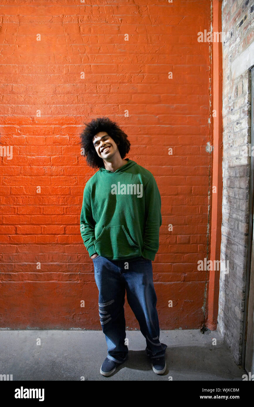 Full length of smiling young man standing in front of orange brick wall ...