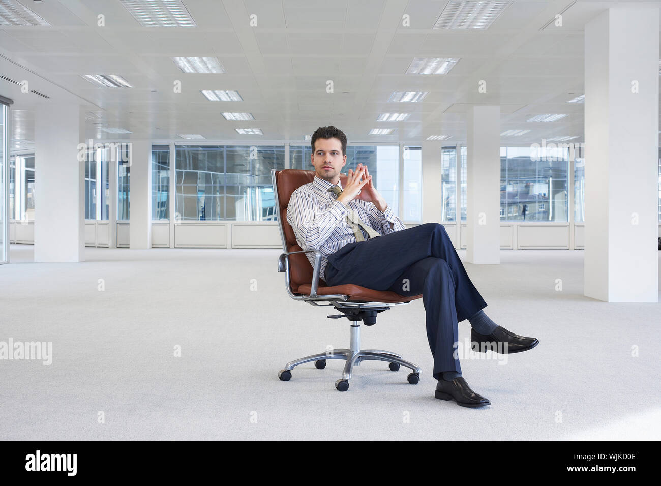 Full length of confident young businessman on chair in empty office ...