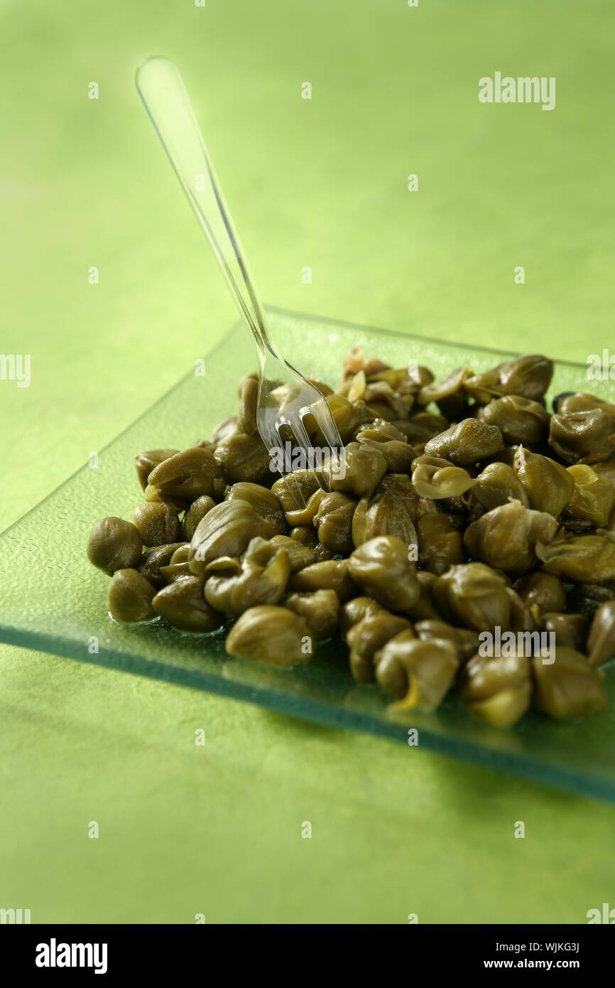 Capers with vinegar snack on a transparent plate, green background ...