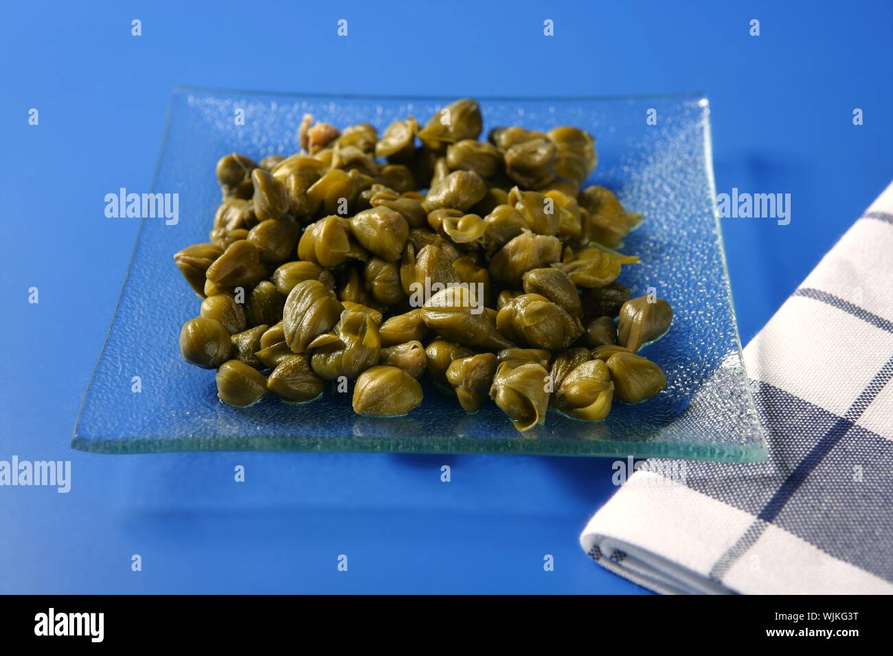 Capers with vinegar snack on a transparent plate, blue background Stock ...