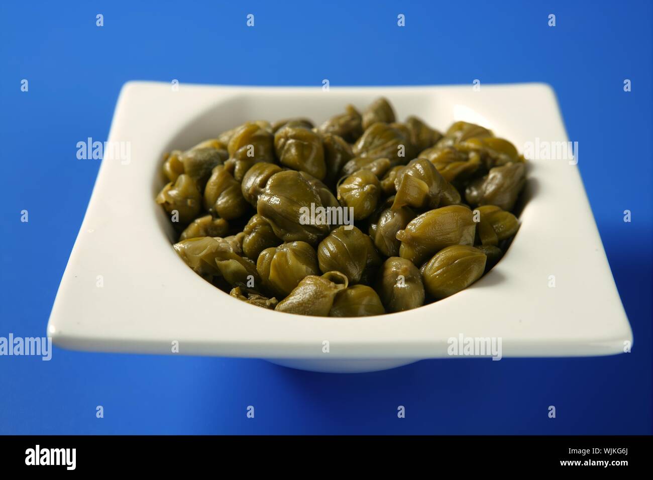Capers with vinegar snack on a white plate, blue background Stock Photo ...