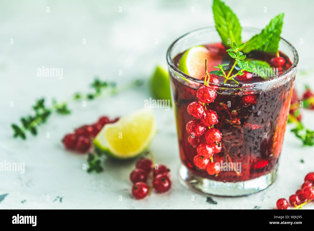 Cold red cocktail with currant, lime, mint, thyme and ice in glass on ...