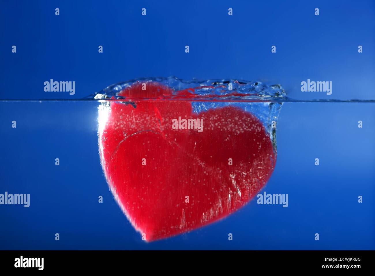 Candy red heart shape sinking into the blue water side view Stock Photo ...