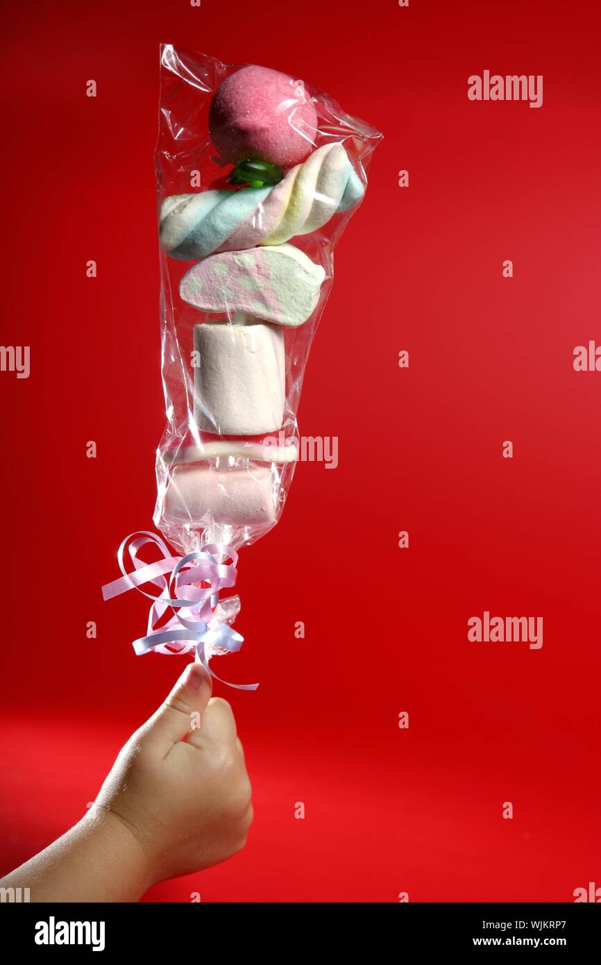 children hand with a stick full of sweet candy over red background ...