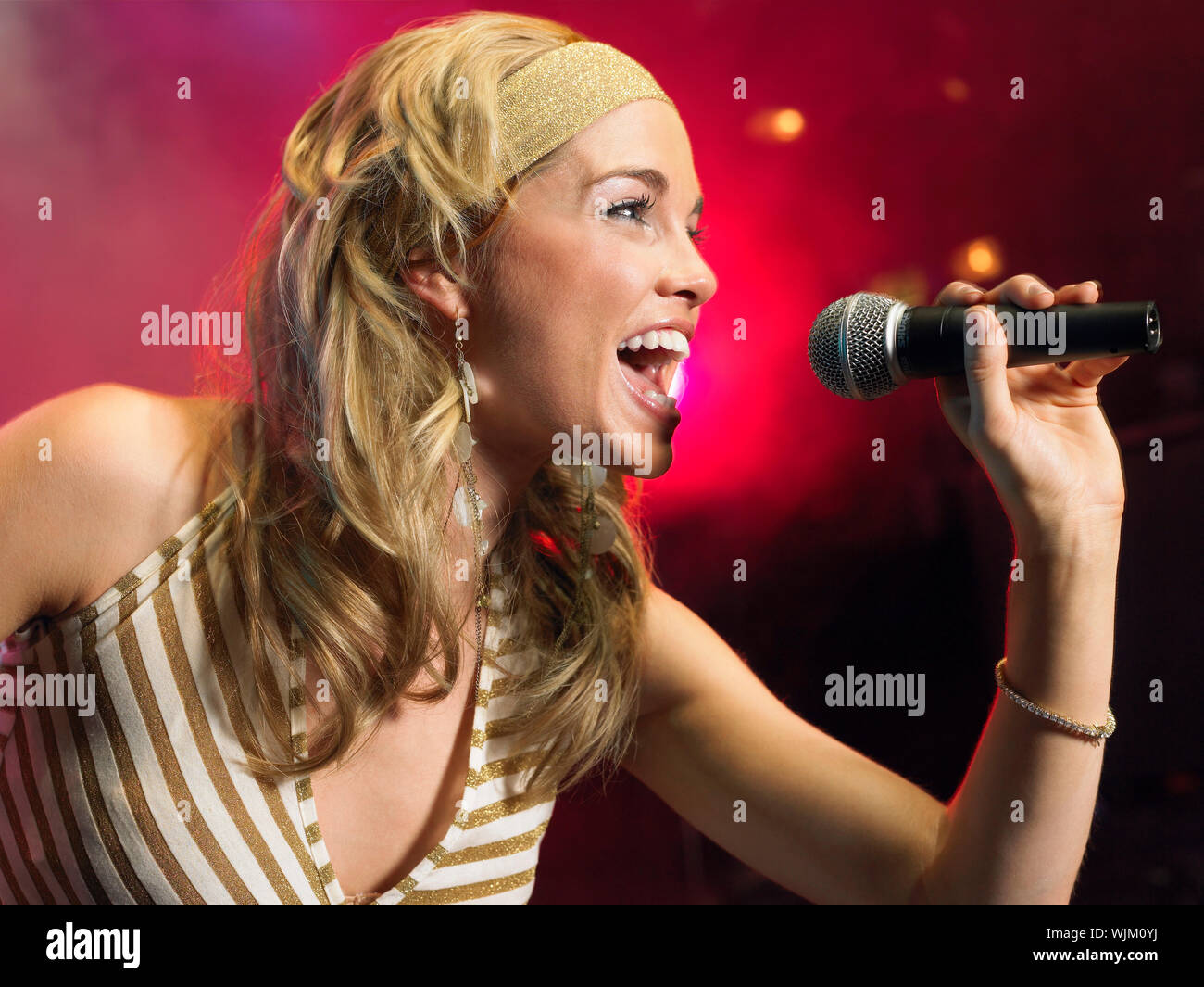 Closeup side view of a beautiful young woman singing into microphone on stage at concert Stock ...