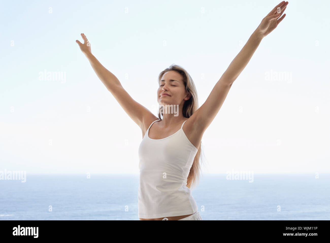 Young woman with arms outstretched and eyes closed standing against ...